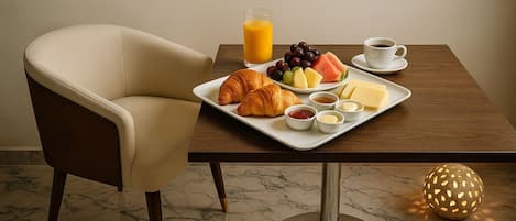 Disposição para o café da manhã com croissants, frutas, queijos e bebidas sobre uma mesa.