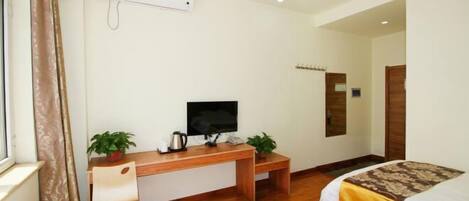 Quarto de hotel com cama, escrivaninha, televisão, cadeira e mesa pequena.