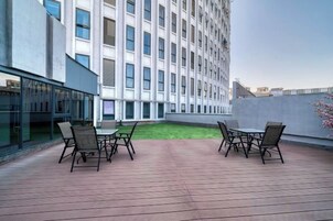 Terraço no telhado com mesa e cadeiras, um edifício ao fundo e uma pequena área gramada.