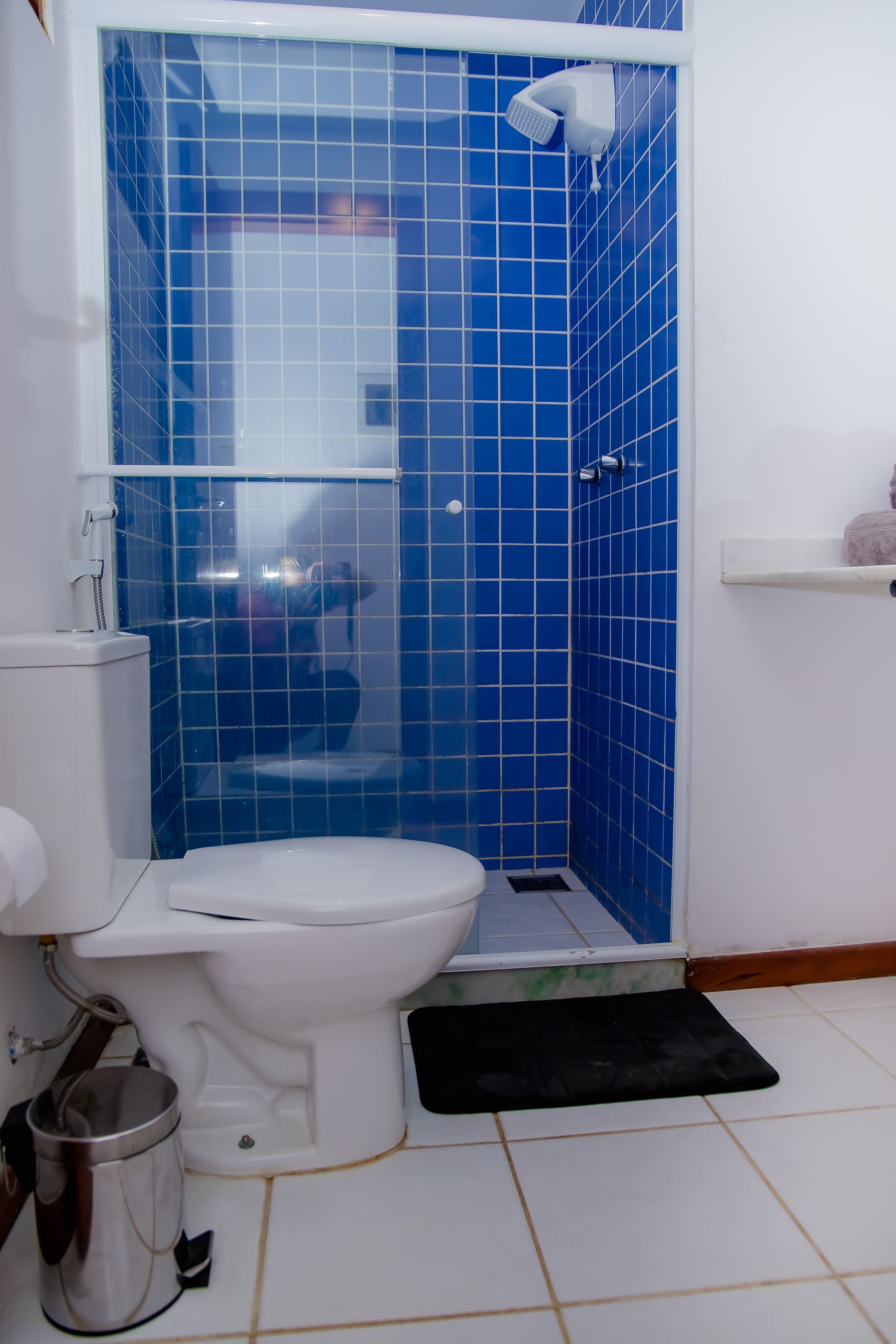 Casa de banho com sanita branca, chuveiro com azulejos azuis e lavatório branco.