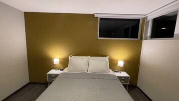 Quarto de hotel com uma cama, duas mesas de cabeceira com abajures, uma janela e um criado-mudo.