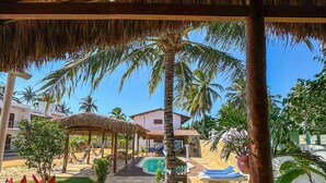 Área externa coberta com piscina, palmeiras e estrutura de telhado de palha.