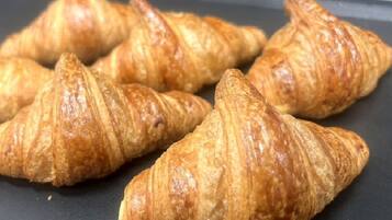 Quatro croissants dourados e crocantes sobre uma bandeja preta.