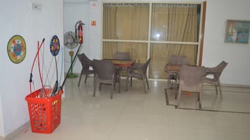 Uma área de refeições com mesa e cadeiras, uma cesta vermelha e um ventilador.
