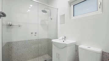 Um banheiro moderno com box de vidro, pia branca e vaso sanitário.