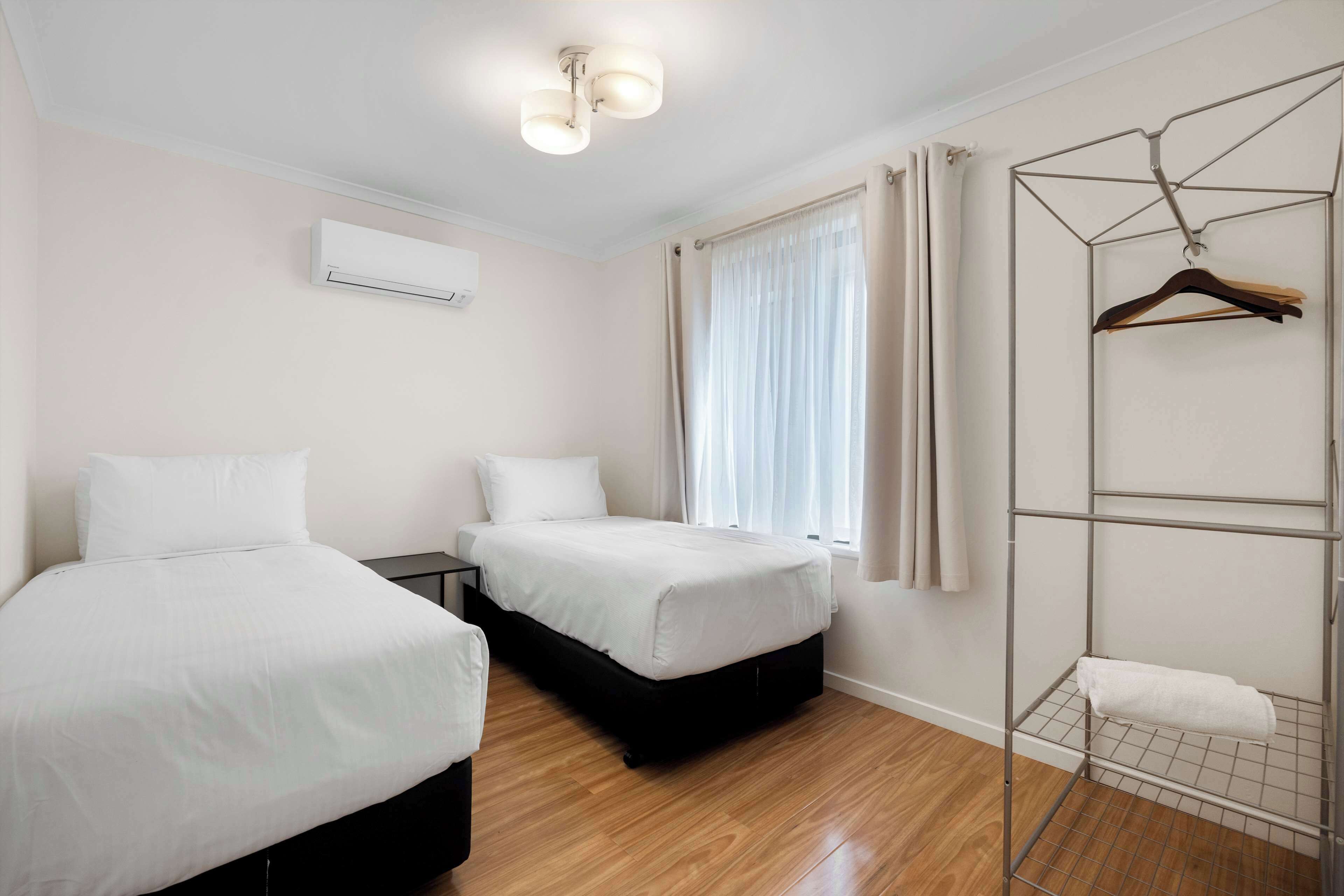 Quarto de hotel com duas camas, um varal de metal e uma janela com cortinas.