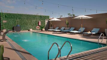 Piscina com espreguiçadeiras e guarda-sóis, um cacto e uma parede verde.