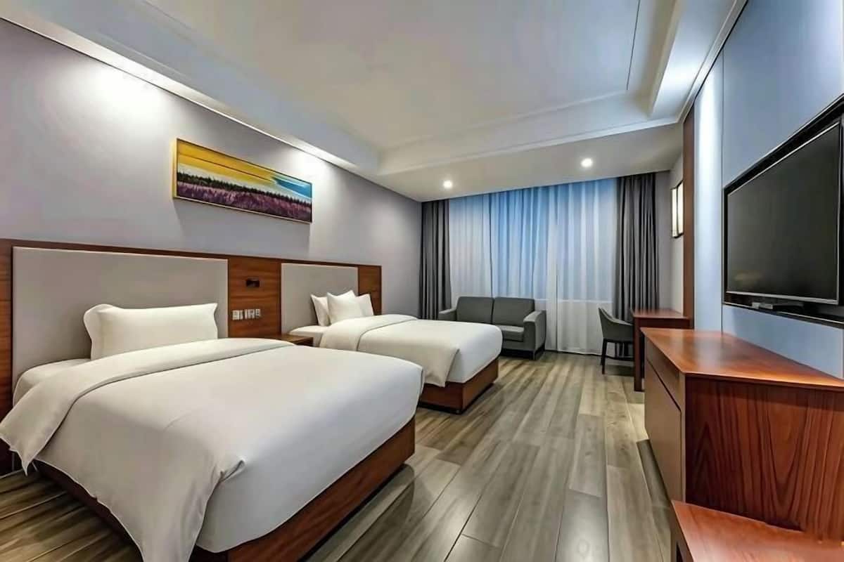 Quarto de hotel com duas camas, televisão, escrivaninha e um quadro na parede.