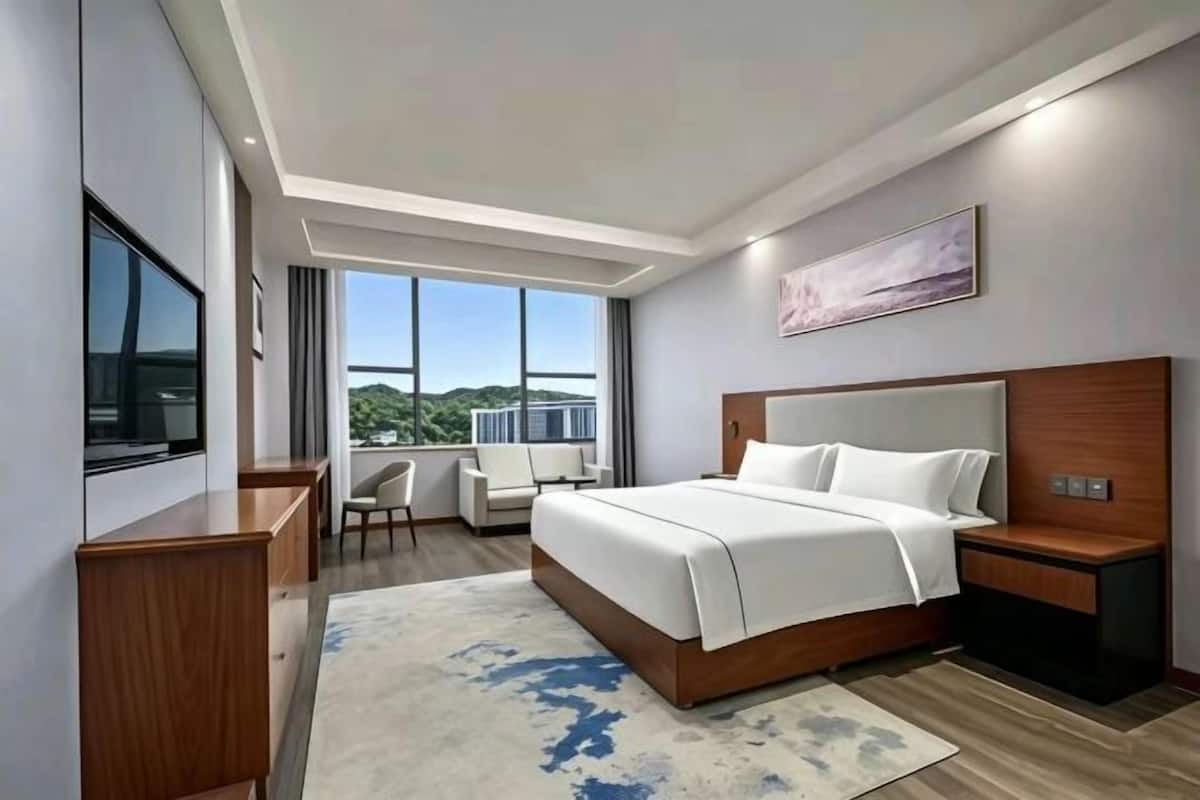 Quarto de hotel moderno com uma cama grande, uma escrivaninha, uma cadeira e uma televisão.