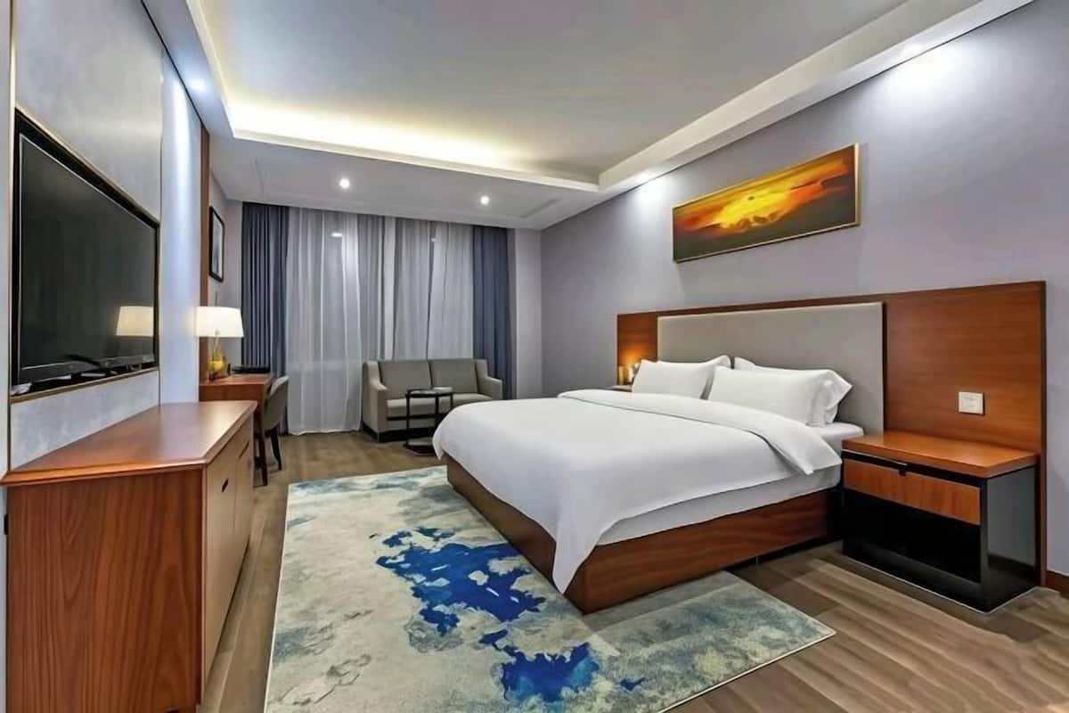 Quarto de hotel com cama, mesas de cabeceira, escrivaninha, cadeira, televisão e um quadro na parede.