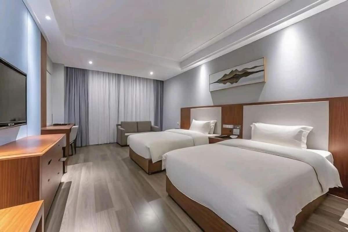 Quarto de hotel com duas camas, uma mesa, uma cadeira, uma televisão e uma cortina.