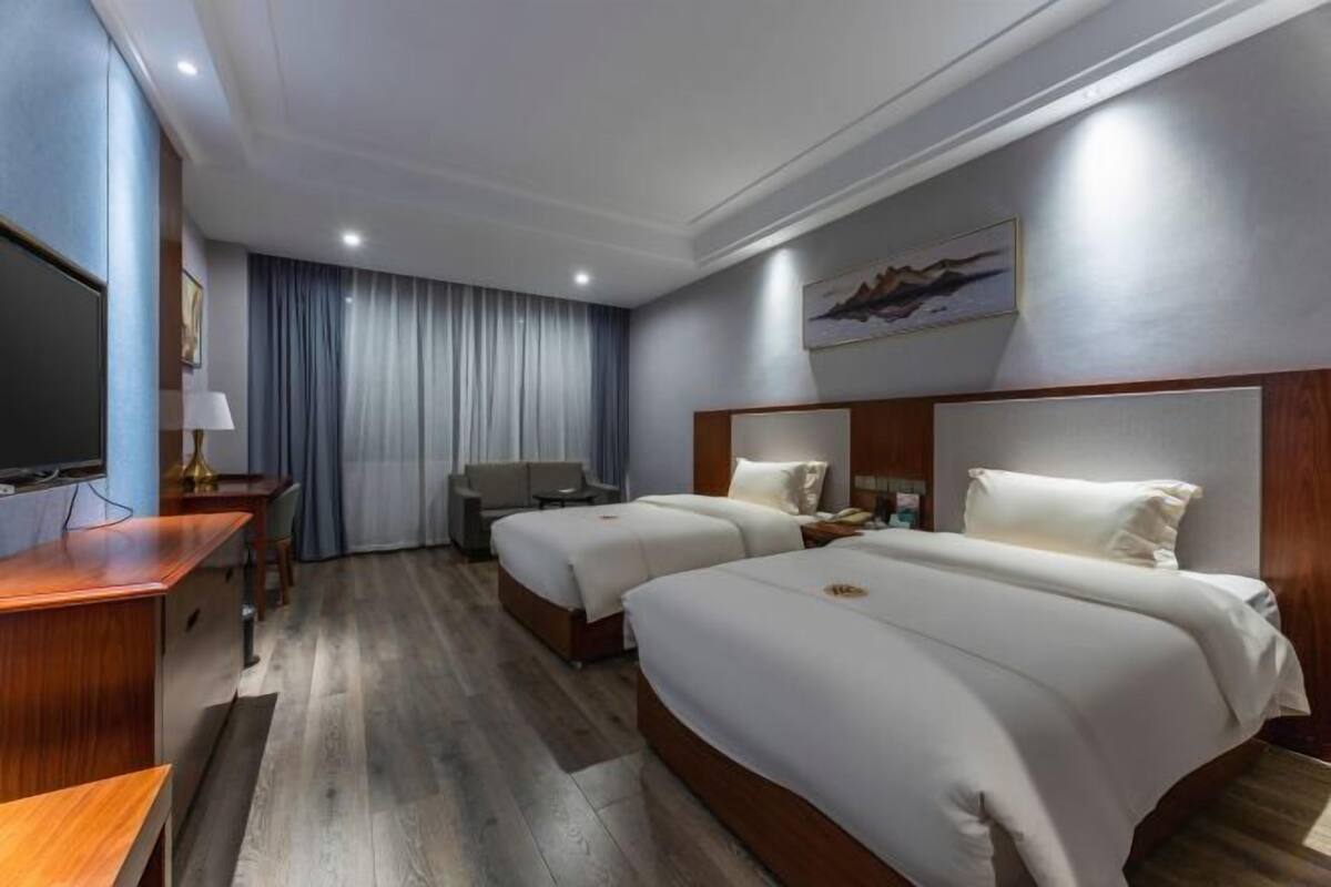 Quarto de hotel com duas camas, uma escrivaninha, televisão e um quadro na parede.