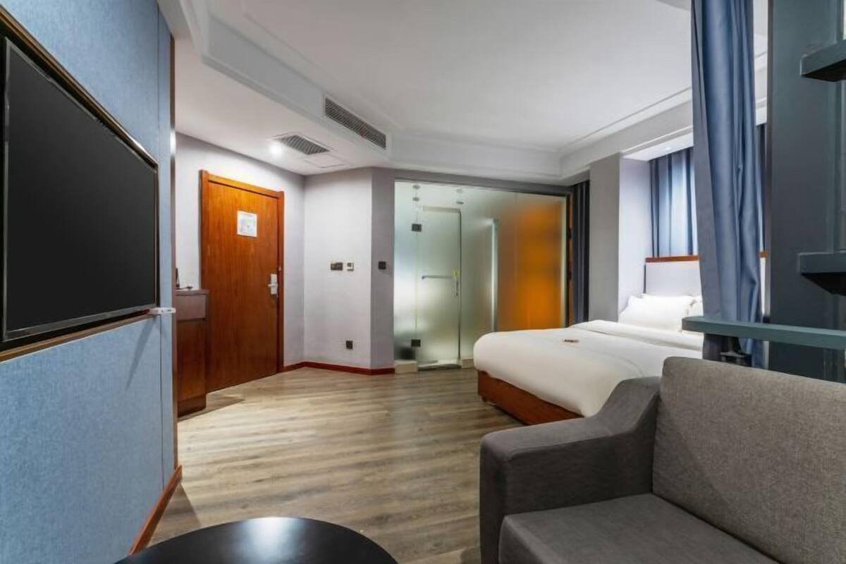 Quarto de hotel com cama, sofá, televisão e porta para um banheiro.
