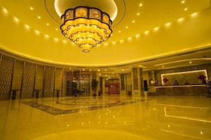 Um hall amplo com um grande lustre, balcão de recepção e piso lustroso.