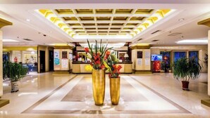 Um hall de hotel com balcão de recepção, dois vasos dourados grandes com flores e um design moderno no teto.