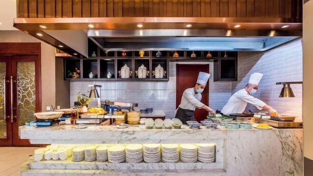 Uma cozinha moderna com chefs preparando comida, bancadas de mármore e diversos utensílios e ingredientes.