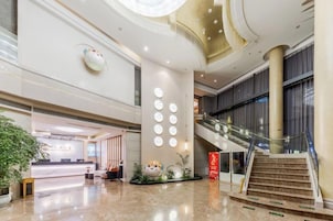 Um hall amplo com balcão de recepção, escadaria e um teto decorativo imponente.