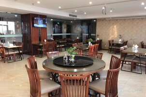 Uma sala de jantar de hotel com mesas redondas, cadeiras de madeira e uma tela de televisão.
