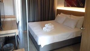 Quarto de hotel com cama, escrivaninha, cadeira, televisão e um quadro na parede.