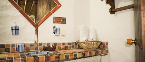 Um banheiro com pia azulejada, espelho, porta-toalhas e um cesto.
