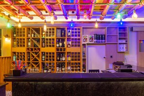 Uma área de bar com prateleiras cheias de garrafas de bebidas, balcão e teto de madeira com canos aparentes.