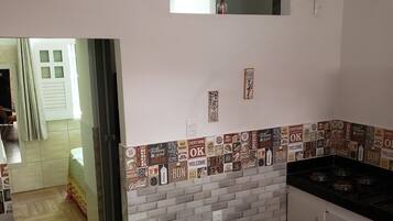 Uma cozinha compacta com área de refeições, com bancada de granito, duas cadeiras laranja, uma pequena janela e painel de parede com padrão de tijolos.