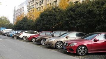 Vários carros estacionados ao longo da rua, com um edifício ao fundo.