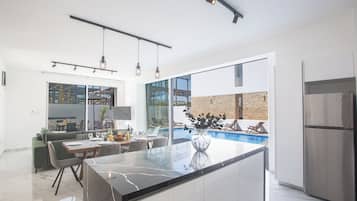 Cozinha moderna com uma ilha grande, área de jantar com mesa de vidro e vista para uma piscina.