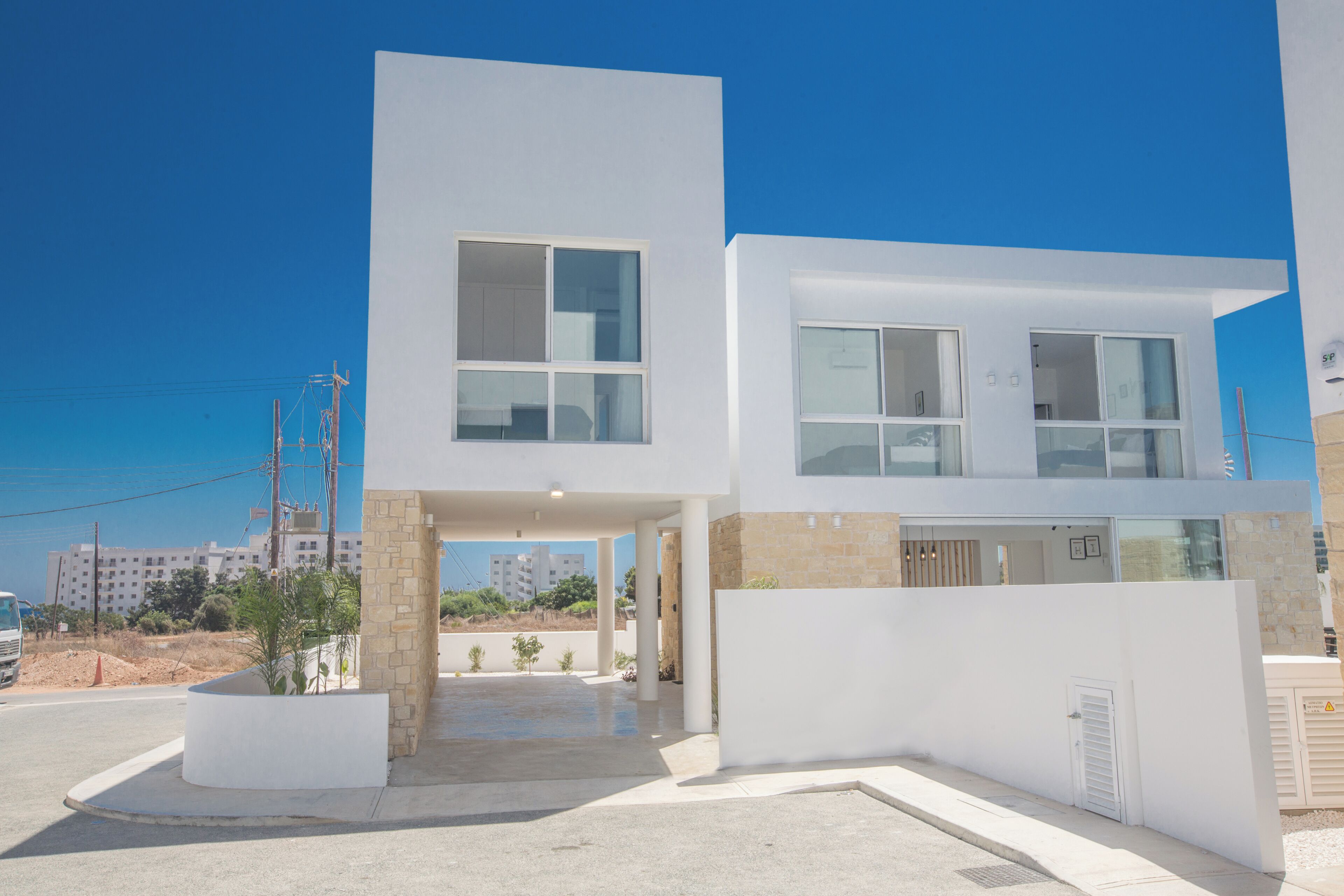 Uma casa moderna de dois andares com fachada branca, janelas amplas e uma entrada com acesso por um caminho de garagem.