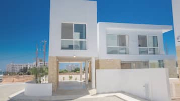Uma casa moderna de dois andares com fachada branca, janelas amplas e uma entrada com acesso por um caminho de garagem.