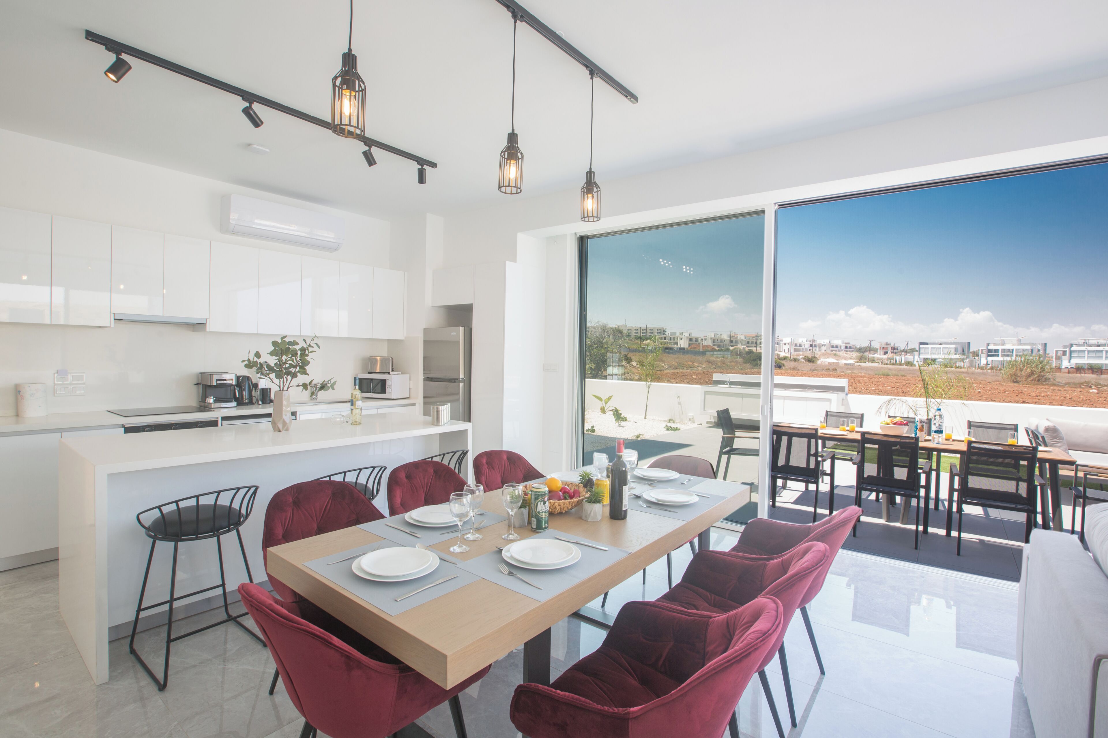 Uma cozinha moderna com armários brancos, um espaço de jantar com cadeiras vermelhas e uma grande janela com vista para a cidade.