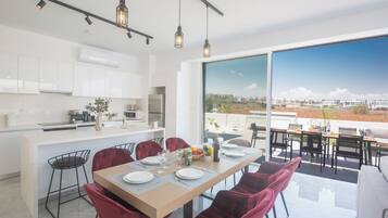 Uma cozinha moderna com armários brancos, um espaço de jantar com cadeiras vermelhas e uma grande janela com vista para a cidade.