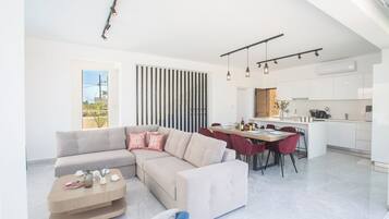 Uma sala de estar moderna com um sofá seccional, uma área de jantar com cadeiras vermelhas e uma cozinha com armários brancos.