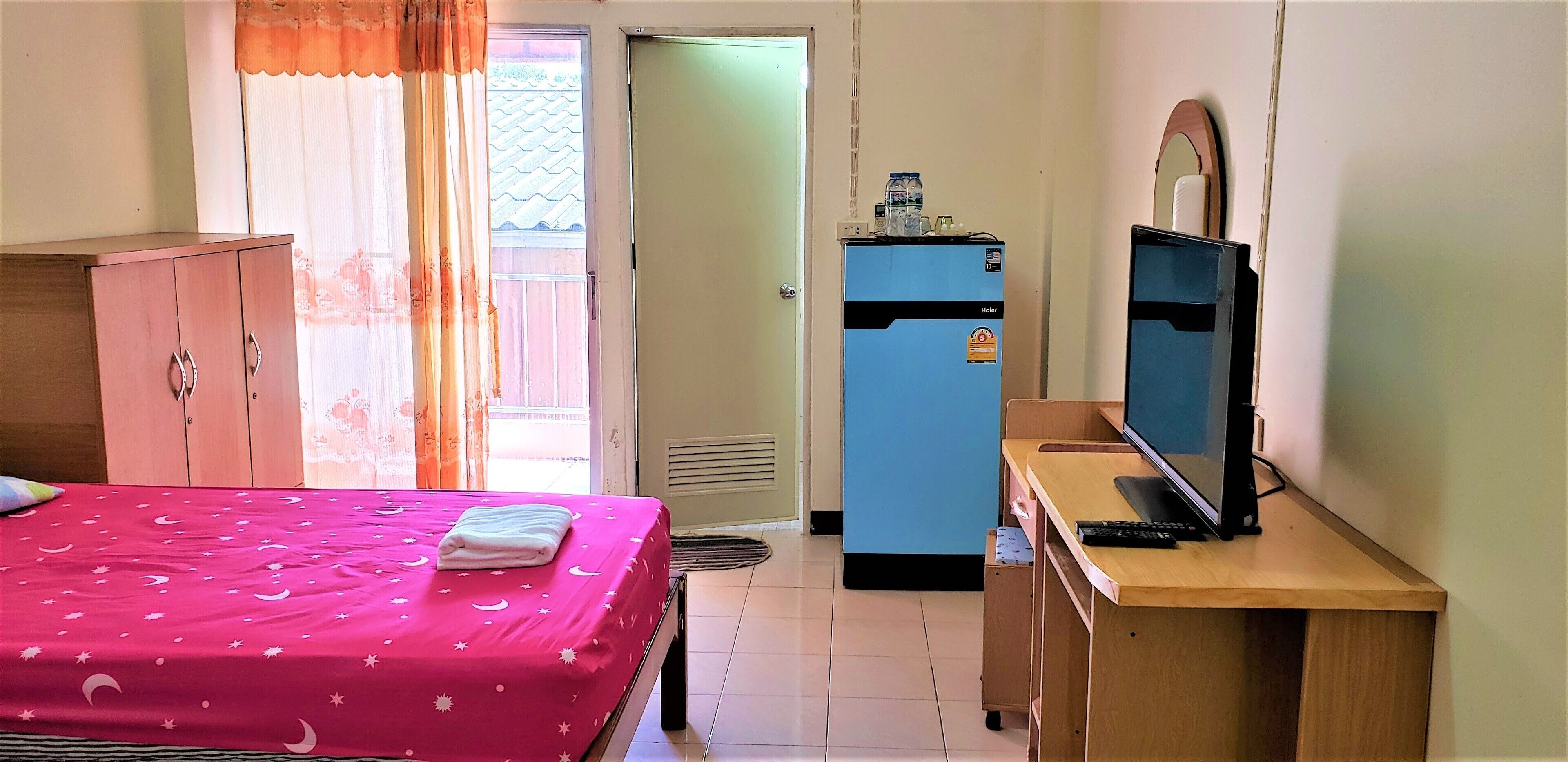 Quarto de hotel com uma cama, uma escrivaninha com computador, televisão e frigorífico.