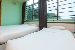 Quarto com duas camas de solteiro, uma janela grande com vista para vegetação e parede verde.