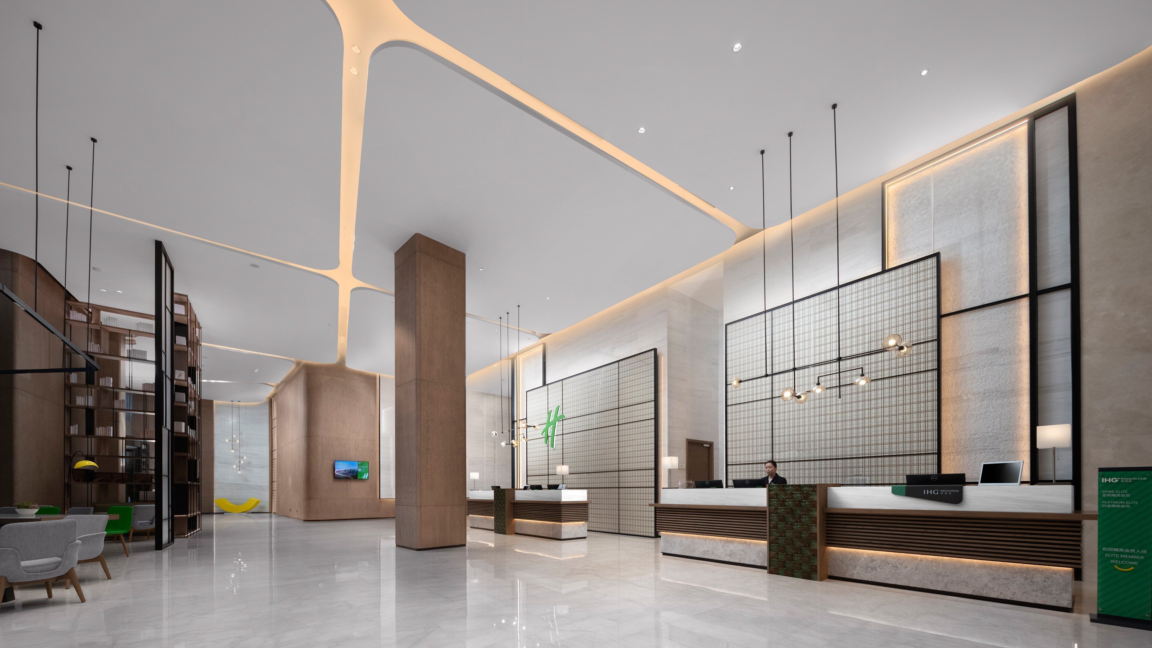 Um lobby de hotel moderno com balcão de recepção, área de estar e um grande painel digital.