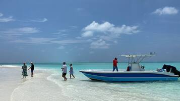 Um barco na praia, com águas azul-turquesa cristalinas e algumas pessoas caminhando por perto.