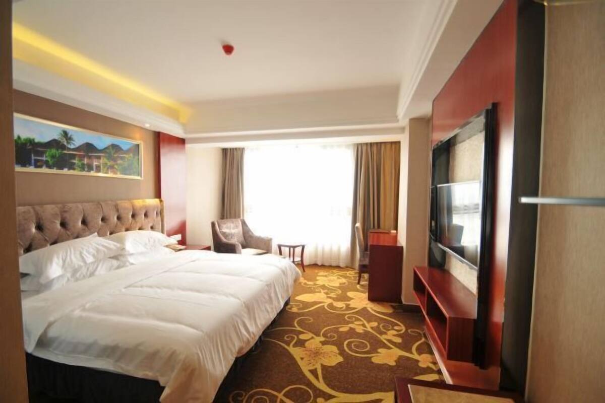Quarto de hotel com uma cama grande, televisão, cadeira e escrivaninha.
