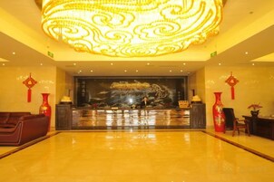 Um hall de hotel com um lustre grande, balcão de recepção e decoração tradicional.