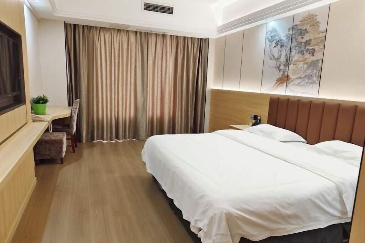 Quarto de hotel com cama, escrivaninha, cadeira, televisão e cortina.