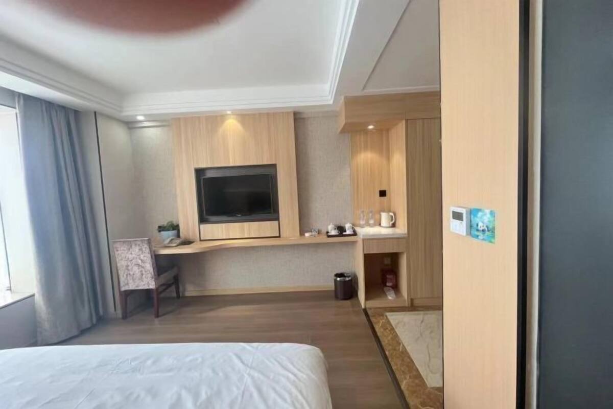 Quarto de hotel com uma cama, uma secretária com televisão, uma kitchenette pequena e um banheiro.