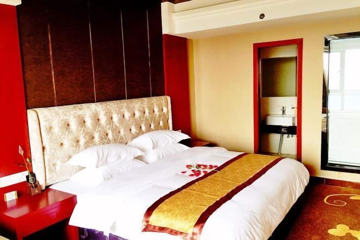 Quarto de hotel com uma cama grande, uma parede de destaque vermelha, um espelho e uma janela.