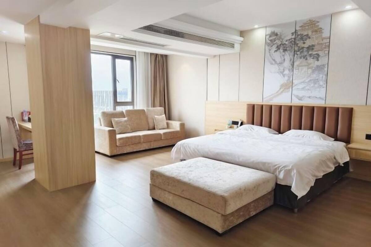 Quarto de hotel moderno com uma cama grande, um sofá, uma escrivaninha e uma janela ampla.