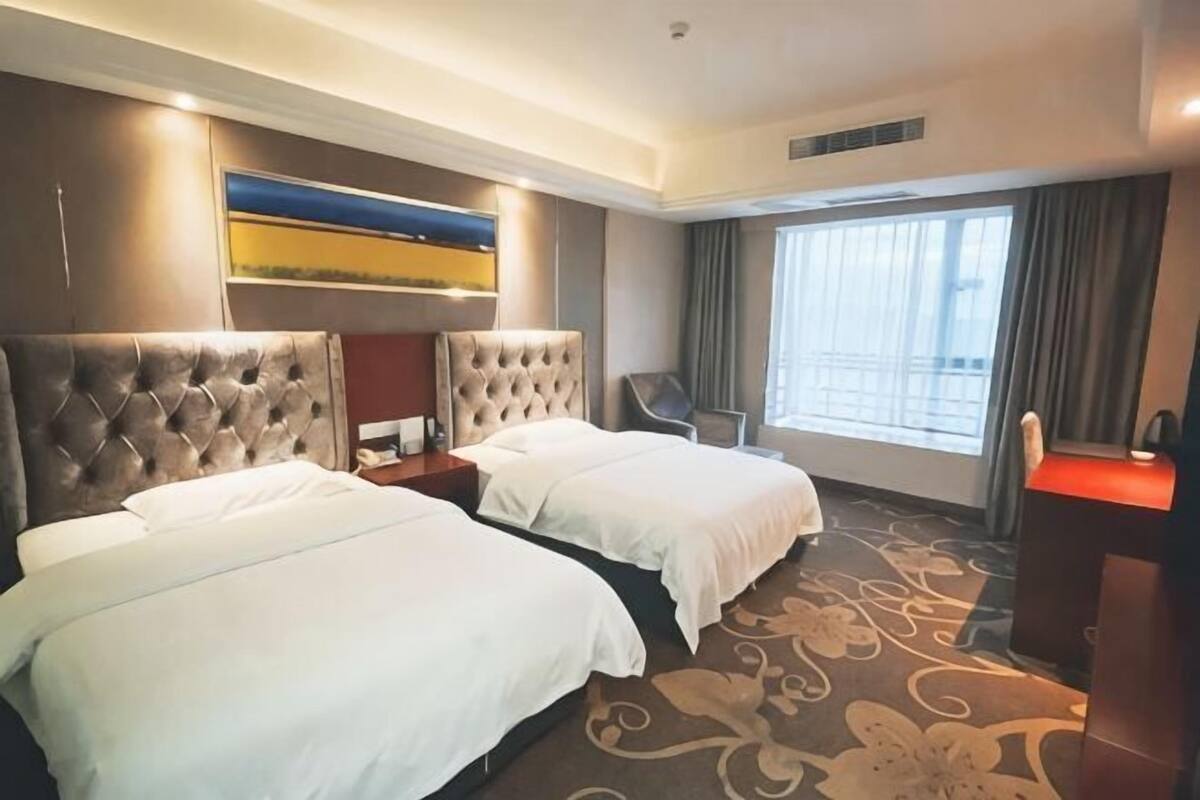 Quarto de hotel com duas camas, televisão de tela plana, escrivaninha e uma janela grande com cortinas.