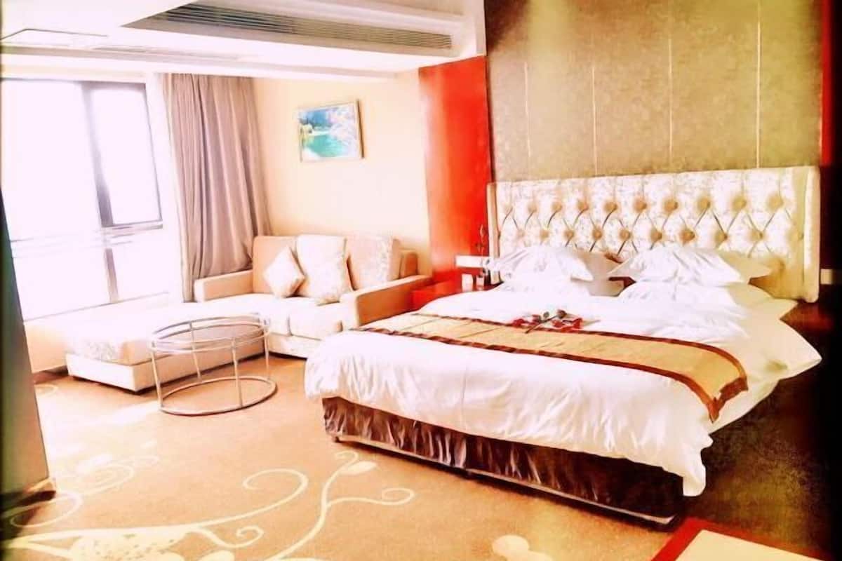 Quarto de hotel com uma cama grande, um sofá, uma mesinha e uma janela com cortinas.