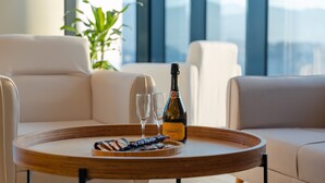 Uma sala de estar moderna com uma mesa redonda de madeira, dois sofás brancos, uma garrafa de champanhe, dois copos e um tabuleiro com aperitivos.