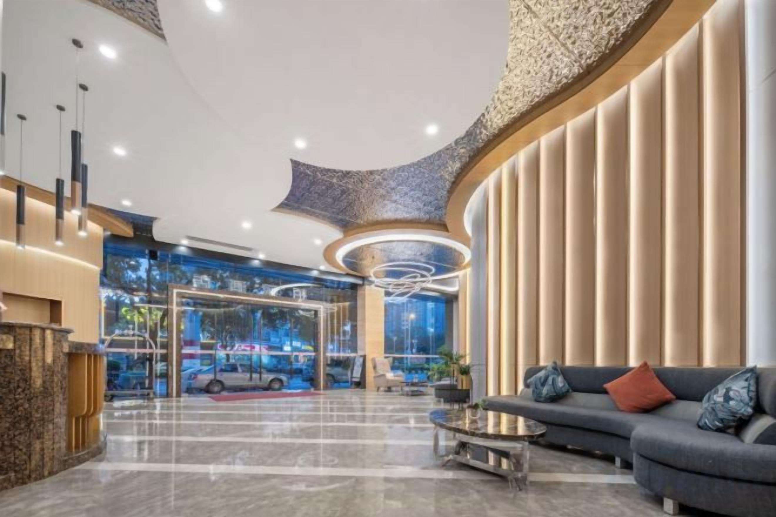 Um lobby moderno com balcão de recepção, área de estar e vista da rua através de portas de vidro.