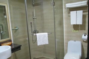 Um banheiro com chuveiro em box de vidro, vaso sanitário e pia com um recipiente decorativo.