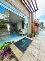 Entrada de hotel com balcão de recepção, área de estar e fachada de vidro transparente.
