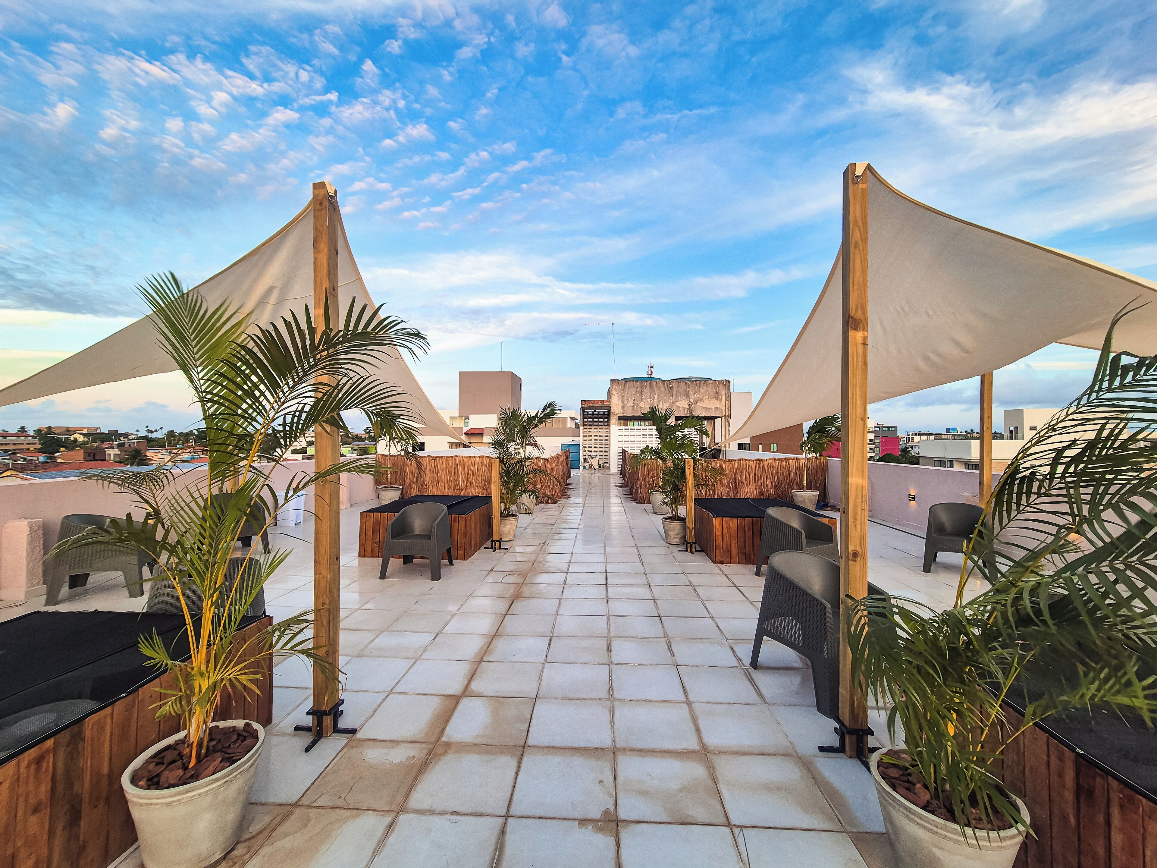 Terraço no telhado com piso de azulejos, plantas em vasos, móveis de madeira e vista para a paisagem urbana.